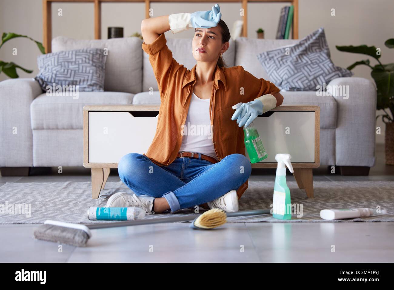 Tired woman, cleaning and sitting on living room floor with detergent ...