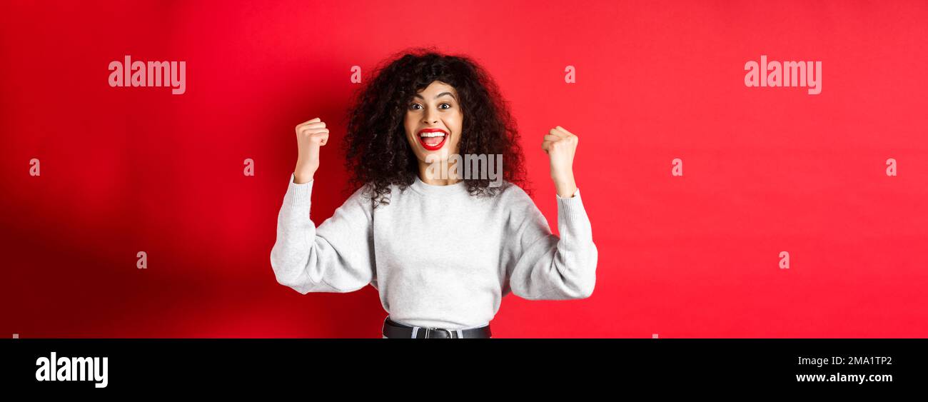Cheerful lucky woman with curly hair, winning prize and scream yes with ...