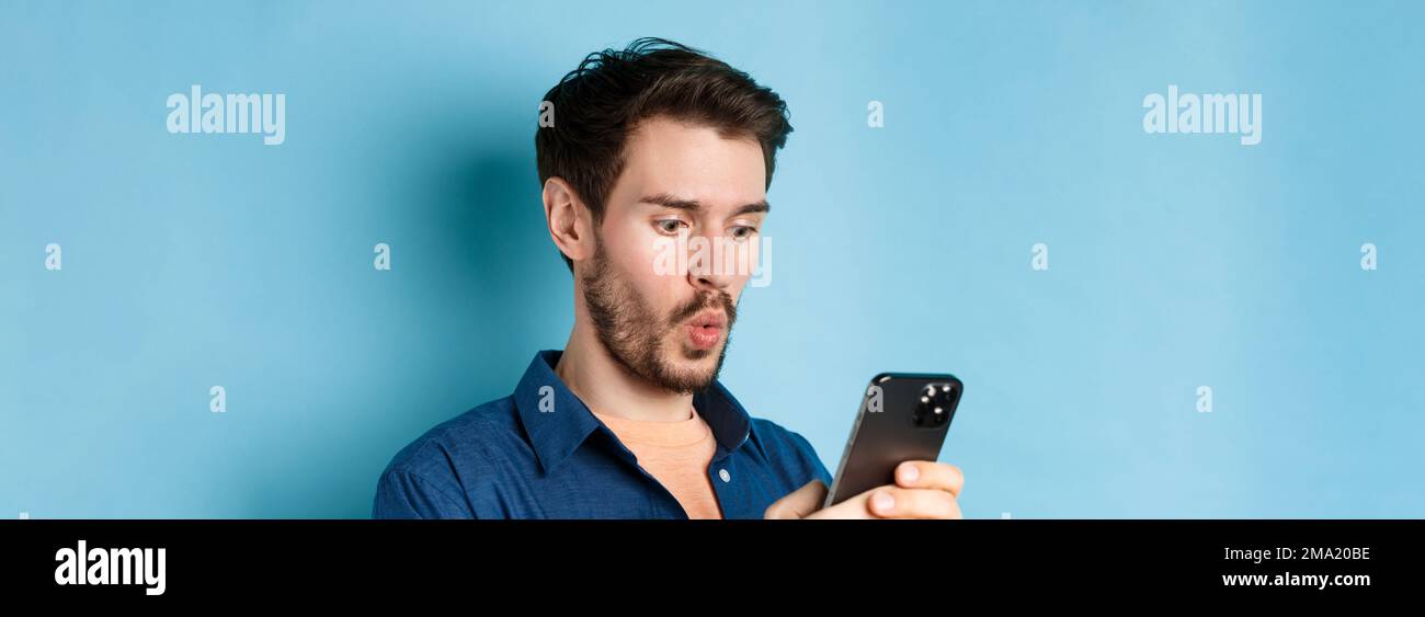Image of impessed young man looking at smartphone and saying wow ...
