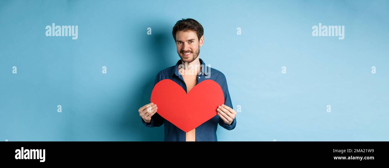 Handsome young man smiling, showing big red heart postcard for ...