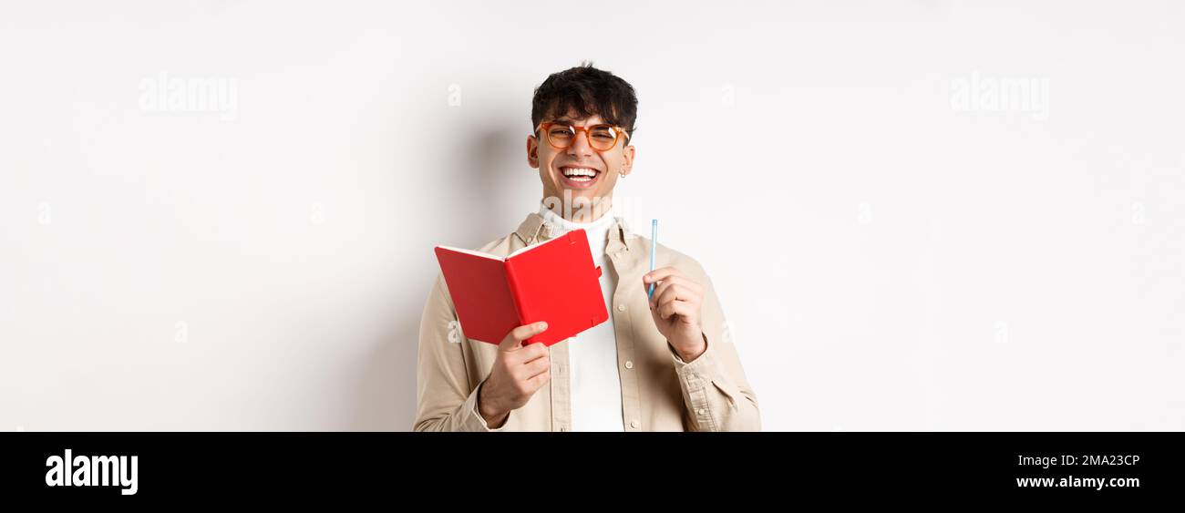 Cheerful young man in glasses laughing and taking notes, writing down ...