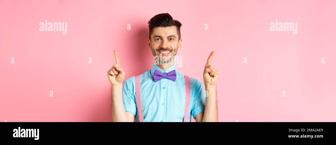 Cheerful handsome guy smiling at camera, pointing fingers up, showing ...
