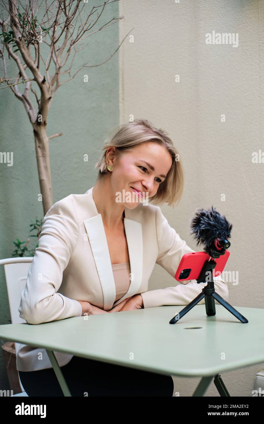 Woman streaming live on her mobile phone while sitting on a table ...