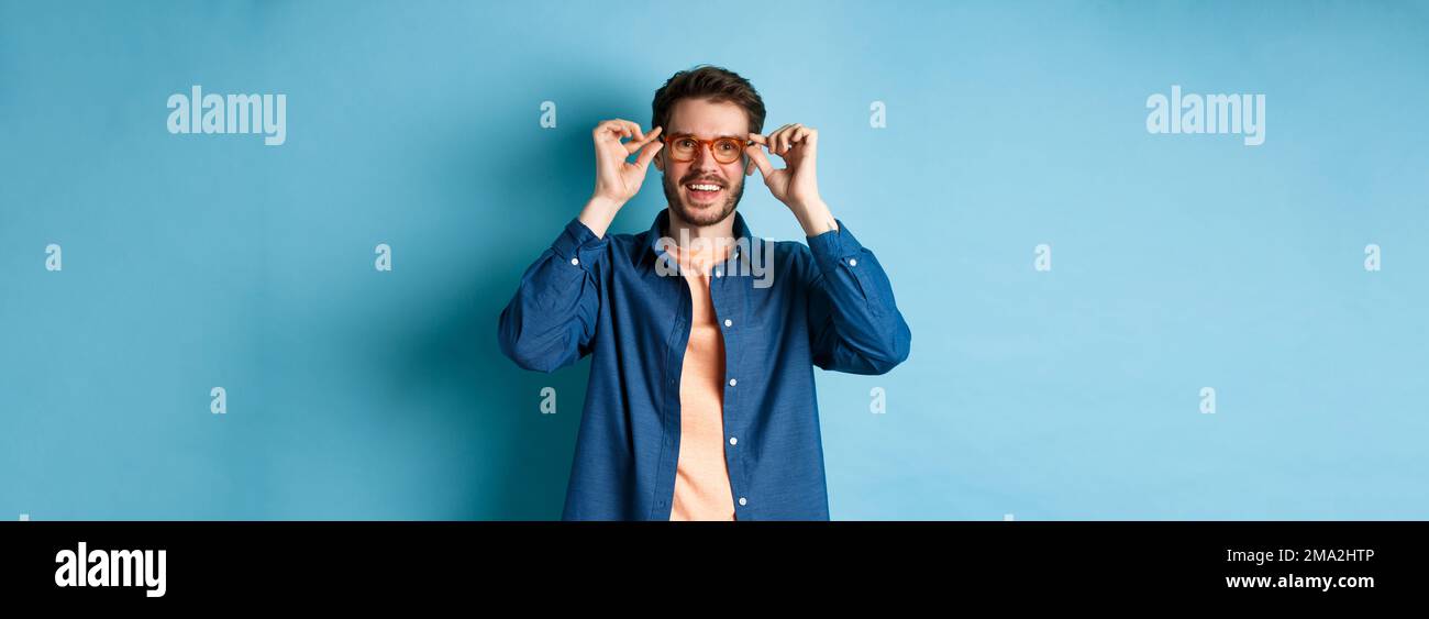 Happy caucasian man trying new glasses and smiling, standing on blue ...