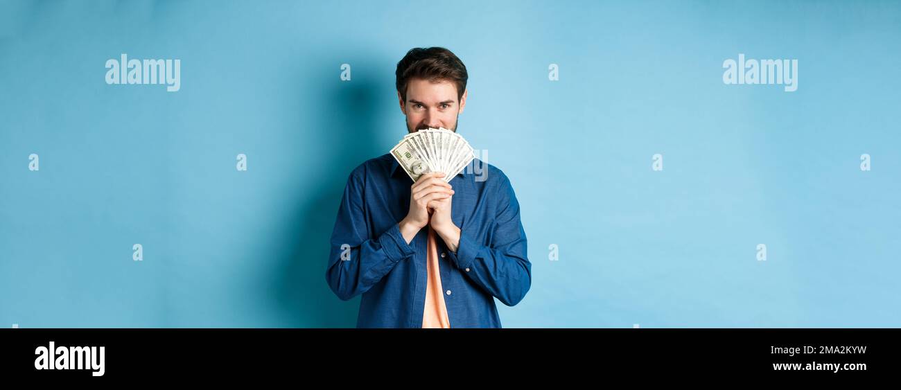 Young man hiding smiling face behind money and looking determined at ...