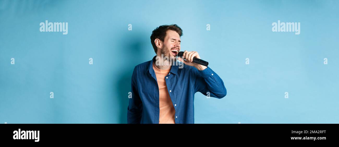 Carefree guy singing karaoke with microphone, perform a song, standing ...