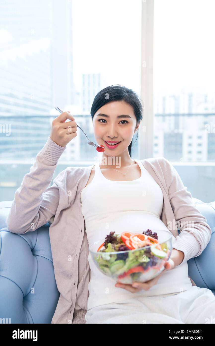 Young women sitting on the sofa eating salad Stock Photo - Alamy