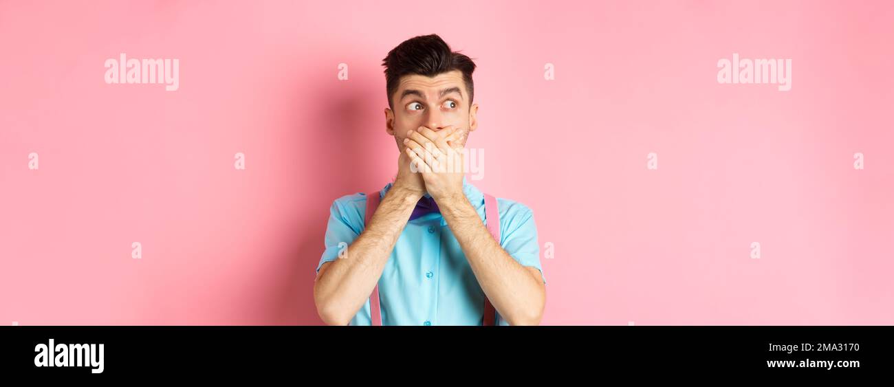 Shocked guy shut mouth, cover lips with hands and looking left ...