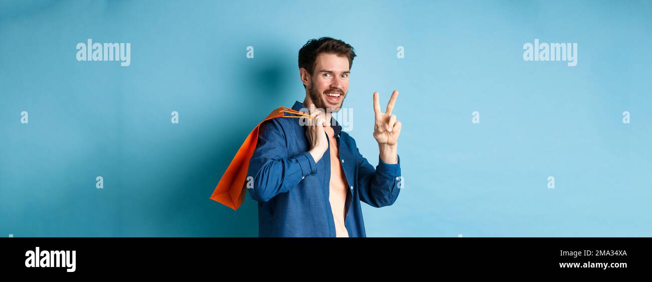 Cheerful guy holding orange shopping bag on shoulder, smiling and ...