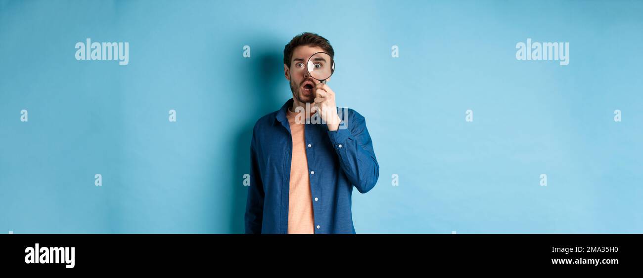 Impressed man look in awe through magnifying glass, drop jaw and stare ...