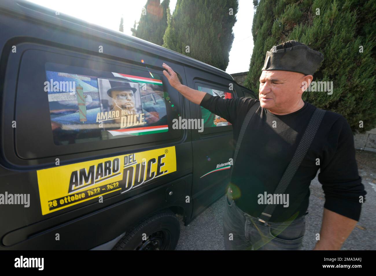 A man flashes the roman salute in front of a car adorned with stickers ...