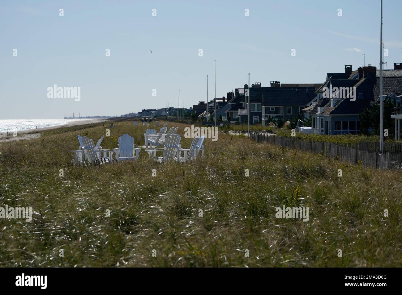 Chairs sit arranged on a high berm that separates the ocean from ...