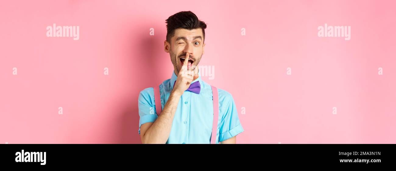 Funny young man planning a surprise, hushing and winking at camera ...