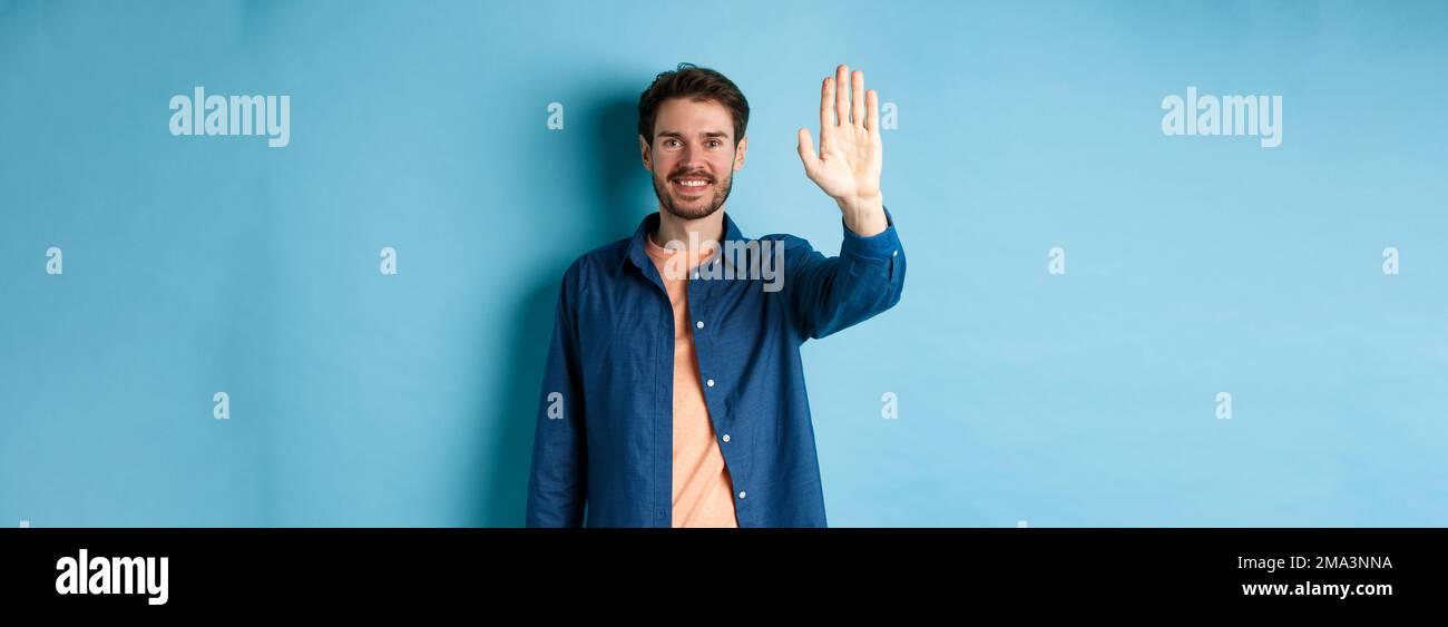 Friendly young man smiling and raising hand up for high five, waiving ...