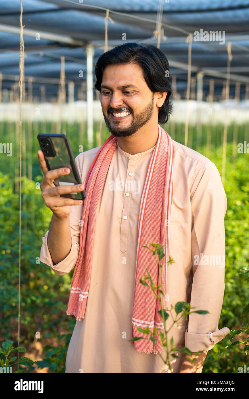 vertical shot of Happy smiling young farmer busy using mobile phone at ...