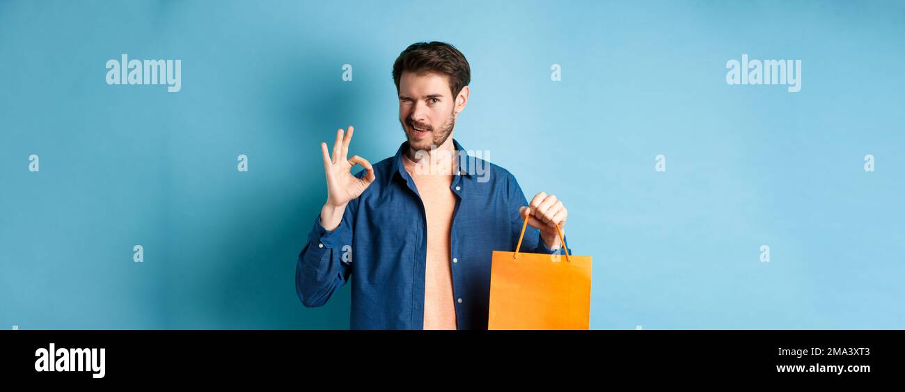 Modern man in casual outfit showing shopping bag and okay sign, winking ...