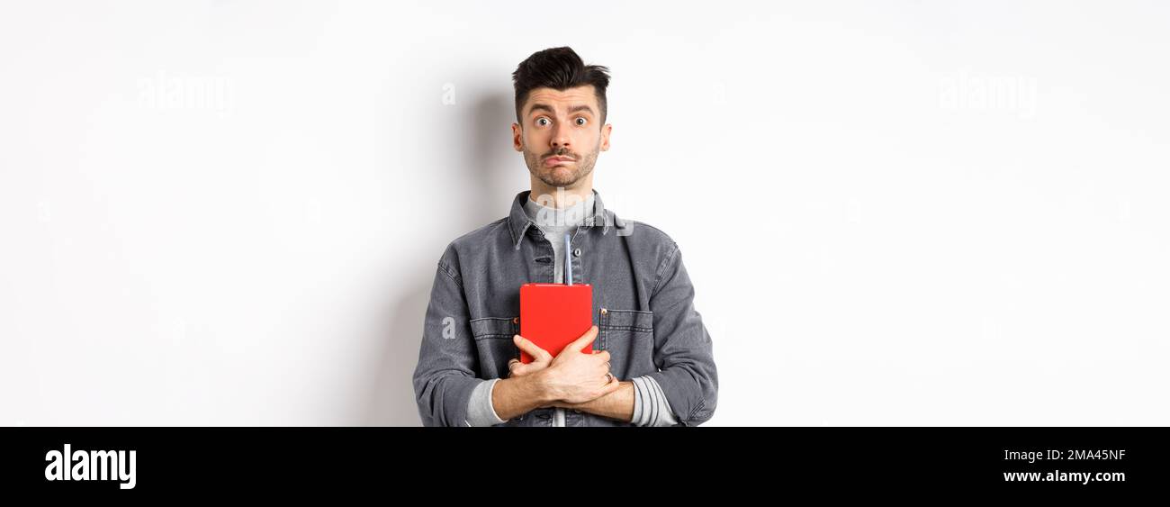 Cute and shy guy hugging his diary, holding red journal and look modest ...