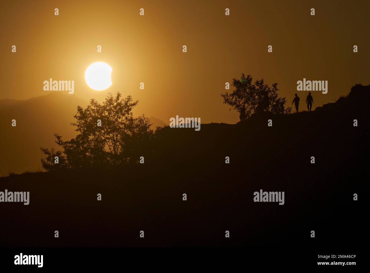 People are silhouetted against a partial solar eclipse seen from ...