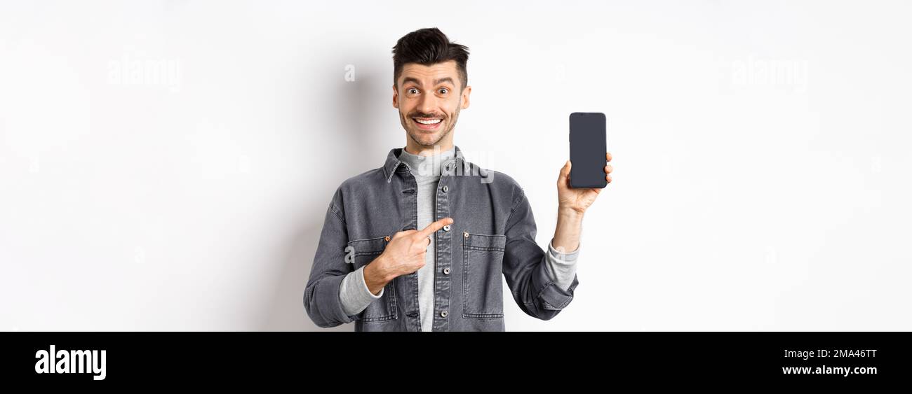 Handsome smiling man pointing finger at smartphone screen, showing ...