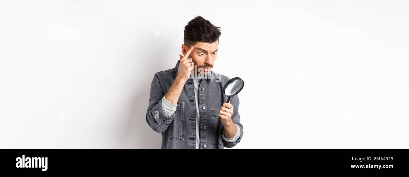 Man looking through magnifying glass and stretching eyelid to see ...