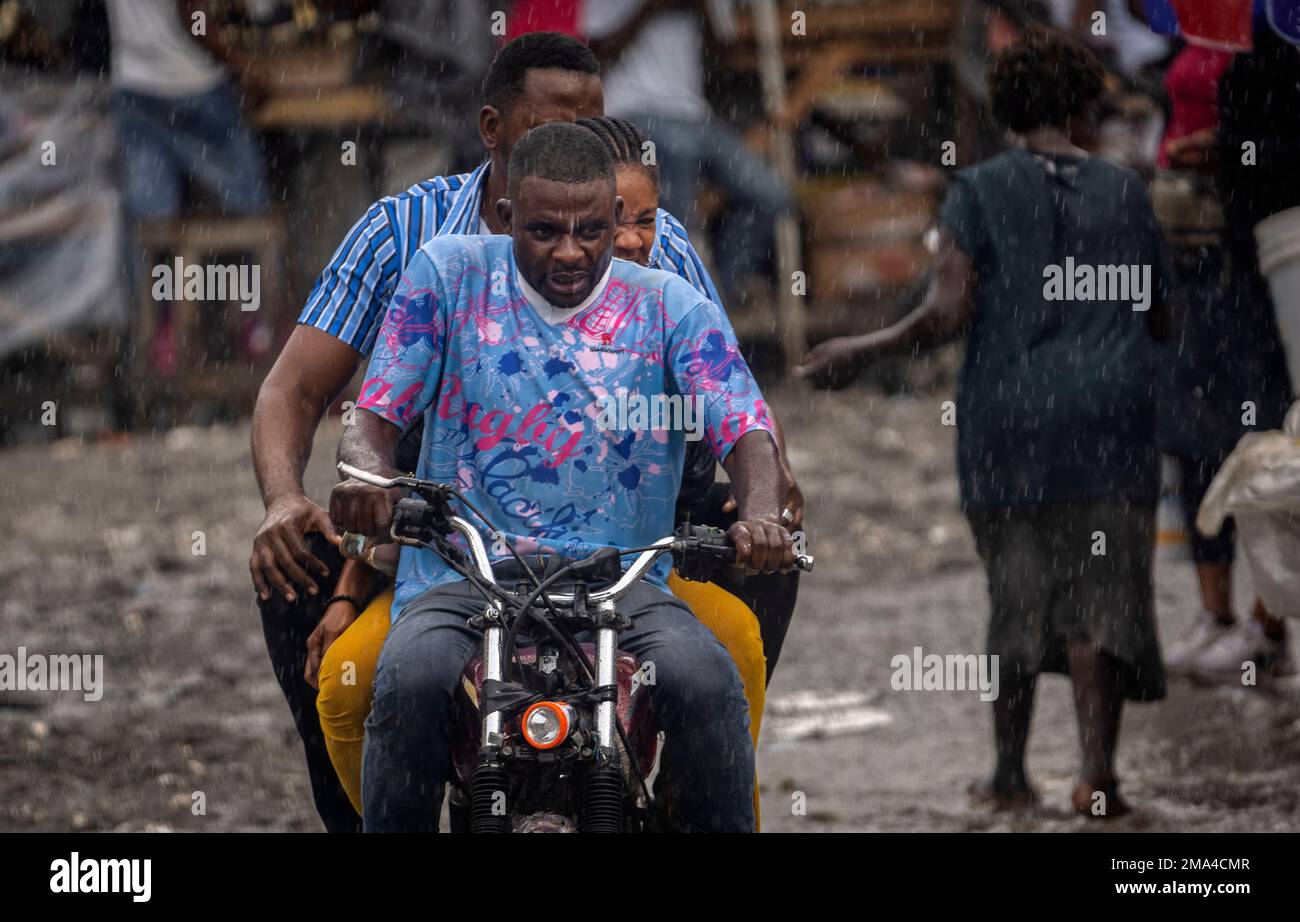 A motorcycle taxi carries two customers under the rain in Port-au ...