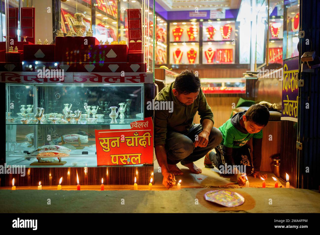 A man and his child light candles outside his store during Tihar ...