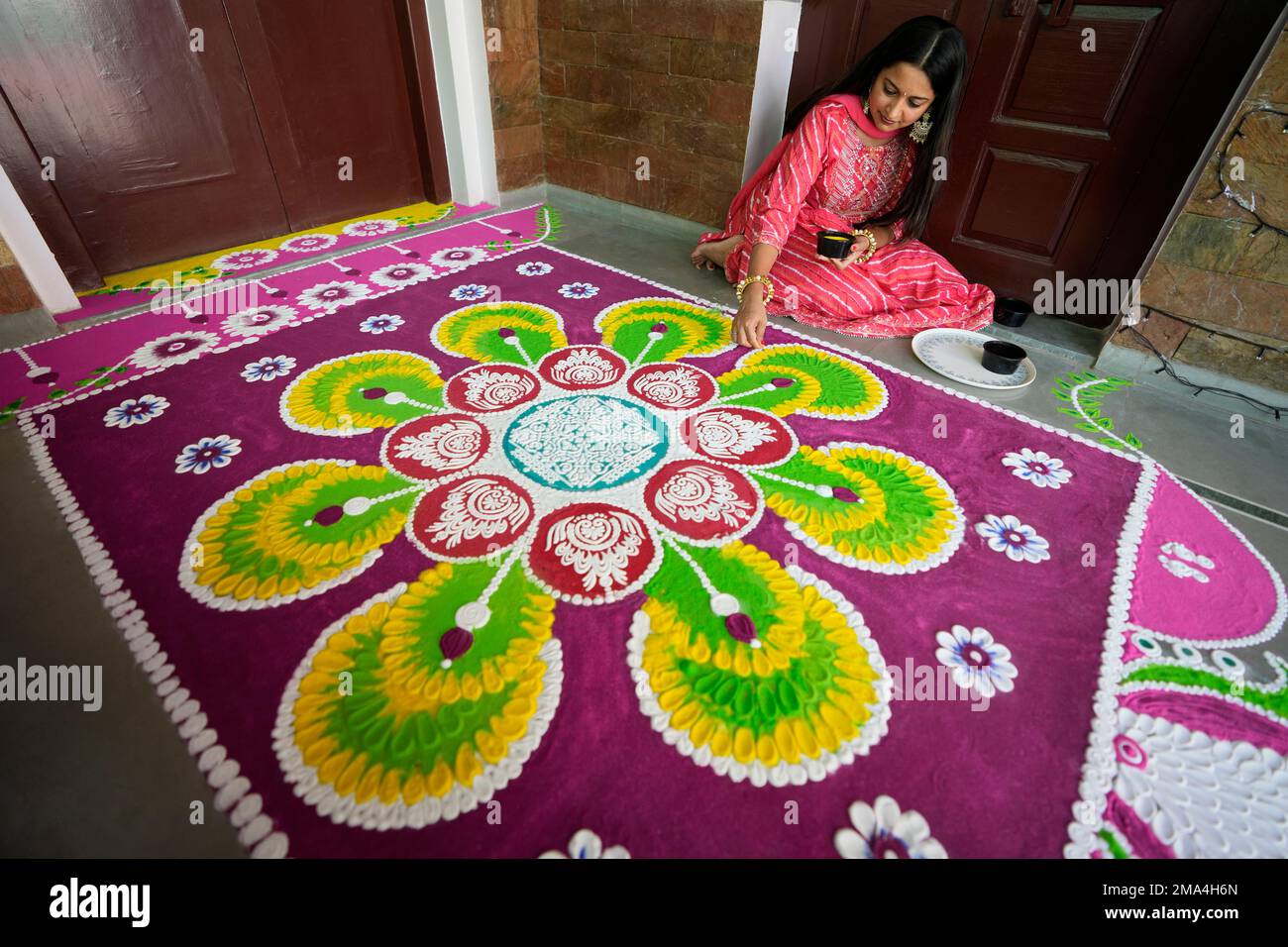 A girl makes a rangoli, a hand decorated pattern on the floor, as part ...