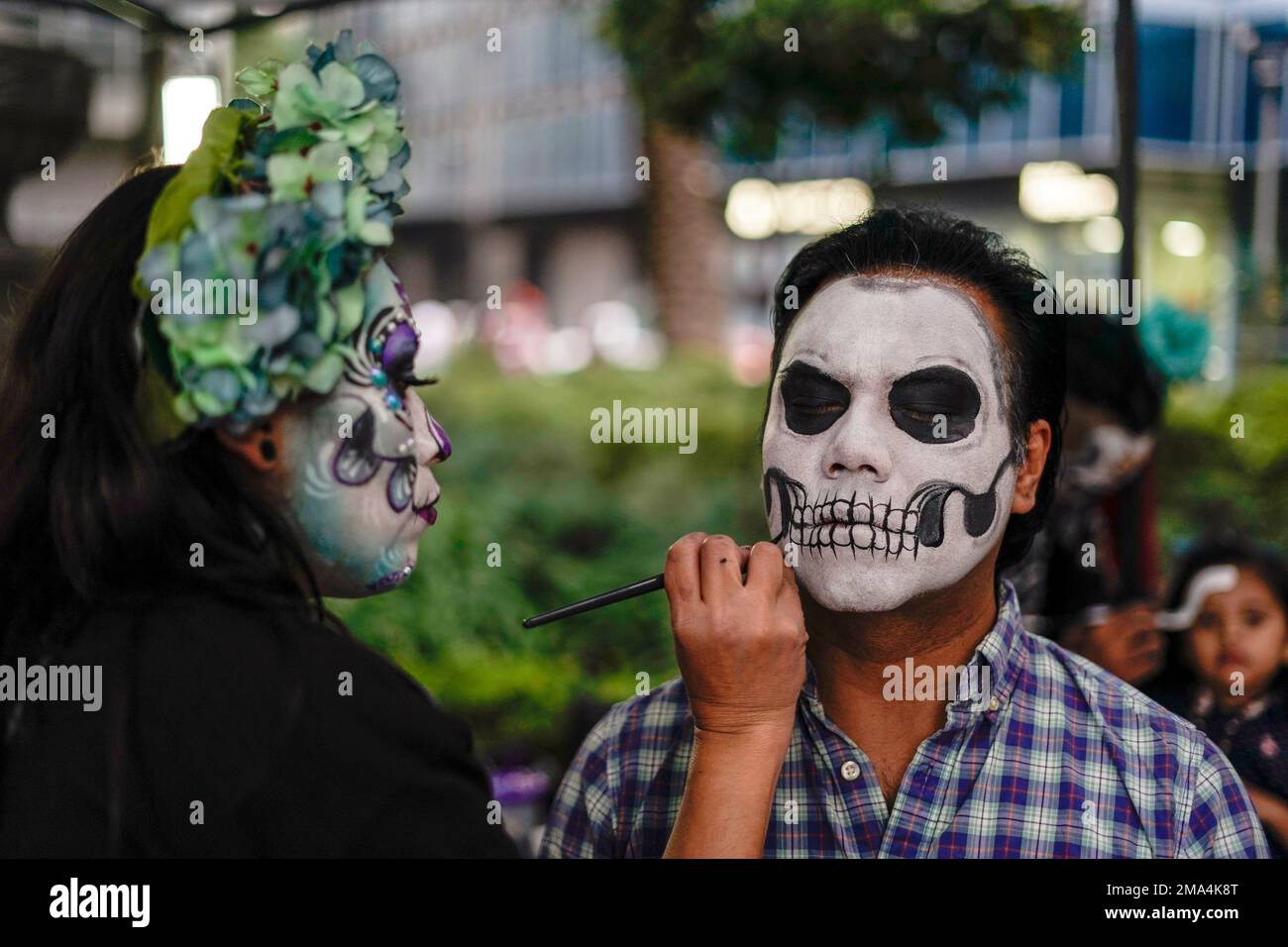 A woman dressed as an iconic Mexican "Catrina" applies makeup to a man ...