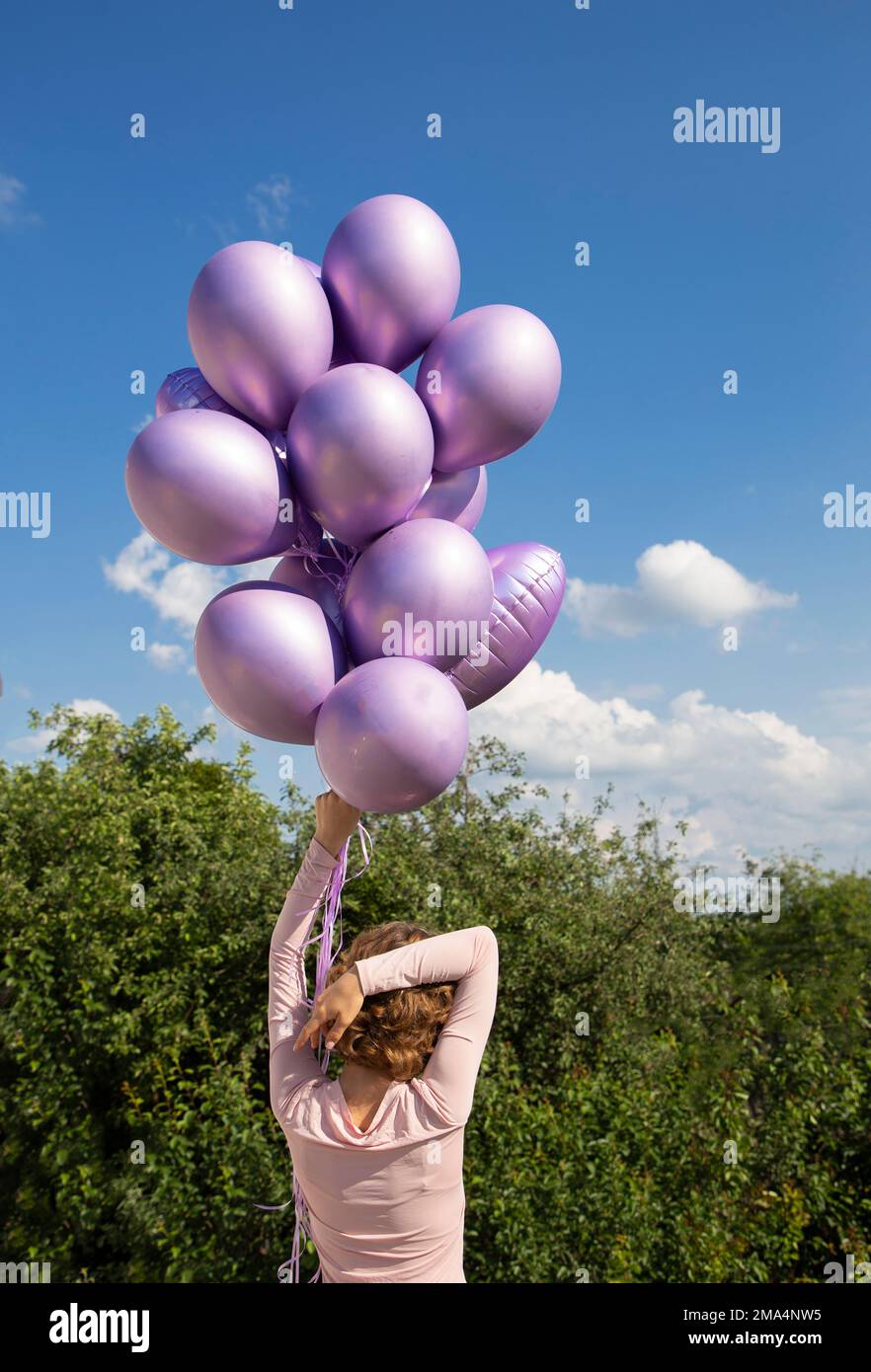 adult girl stands with her back with a bunch of purple helium balloons ...