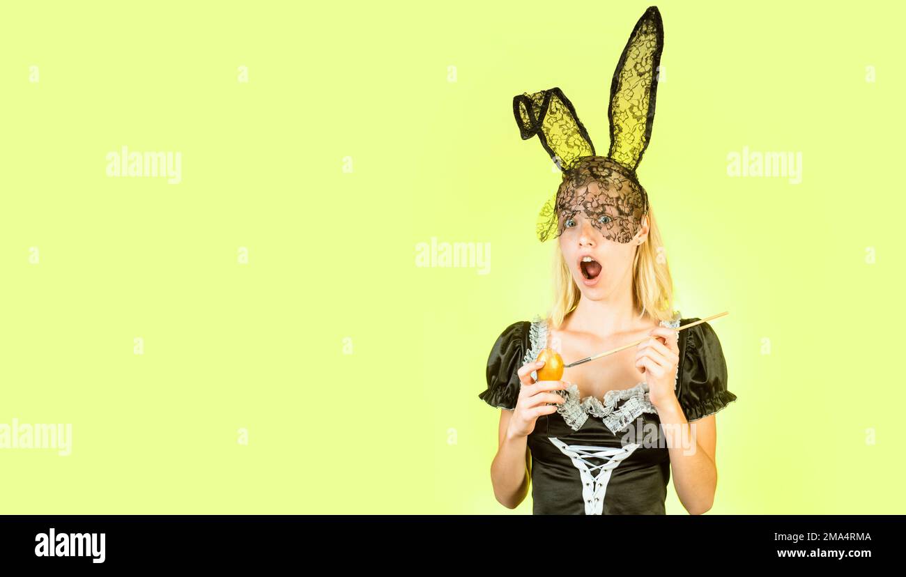 Easter bunny looks surprised at camera drawing golden paint Easter egg ...