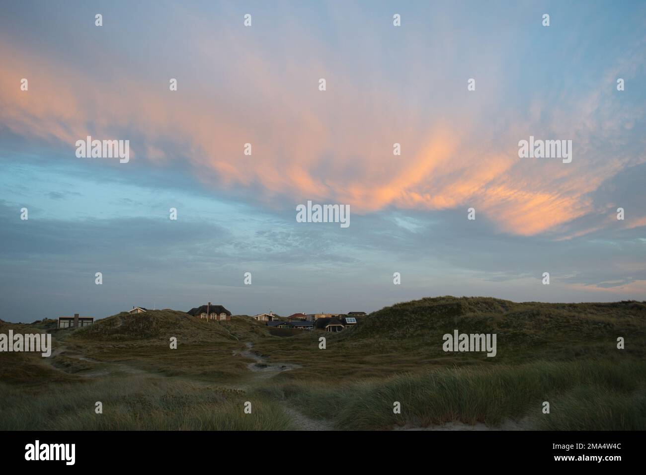 A grass terrain with houses and hills against the colorful sky during a ...