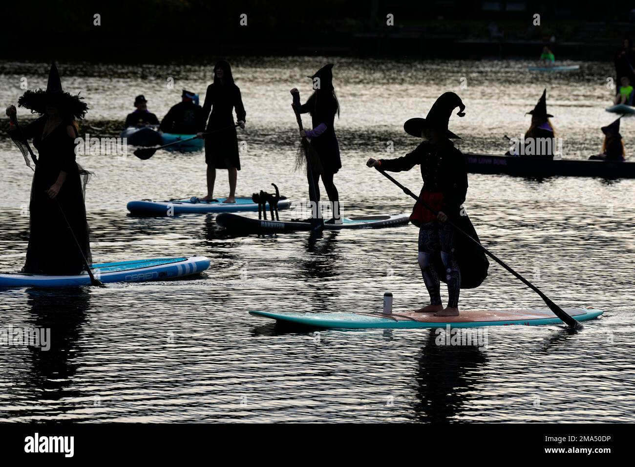 Participants dressed as witches ride paddleboards during the Medford ...