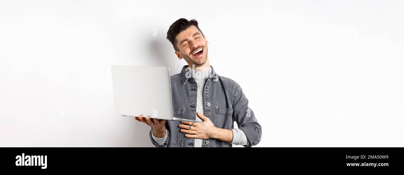 Image of happy guy laughing at funny video on laptop, touching belly ...