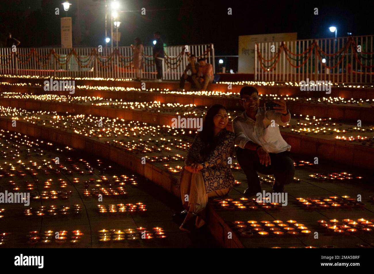 People pose for a selfie sitting by lamps lit to celebrate Diwali ...