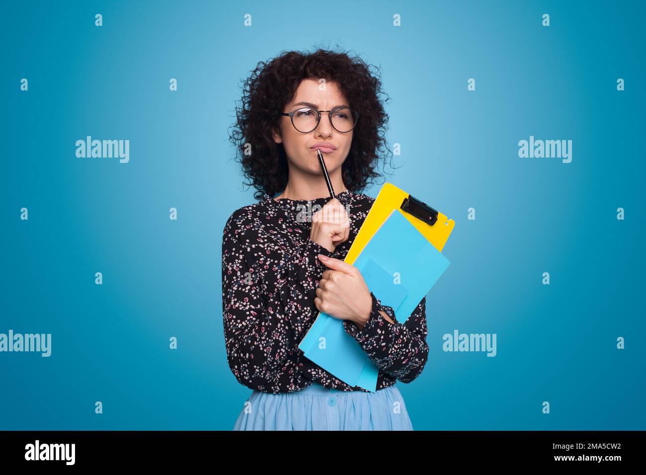 Young curly-haired student woman isolated on blue background having ...