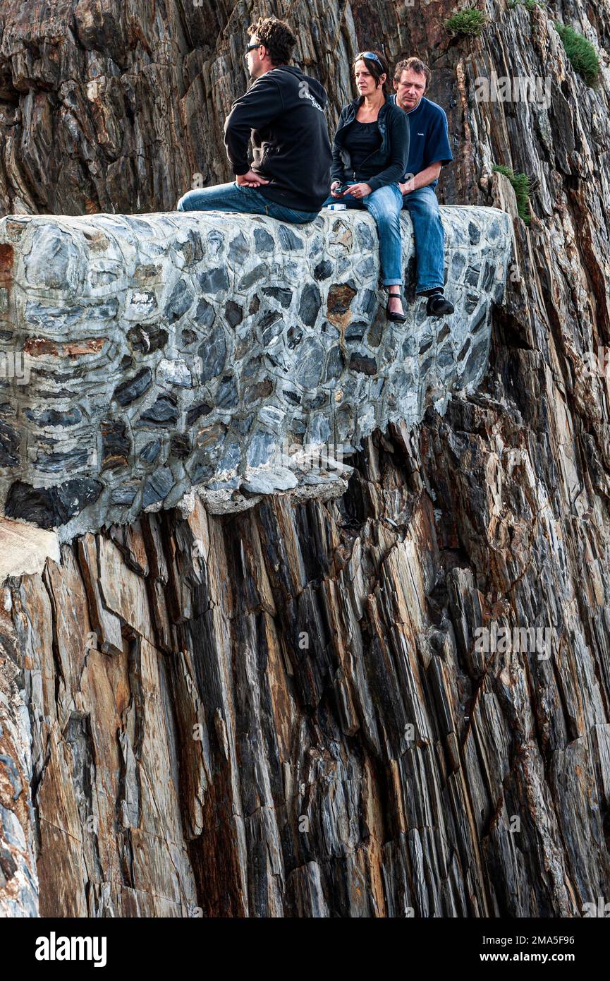People sitting on a natural rock bench next to the cliffs of the Côte ...