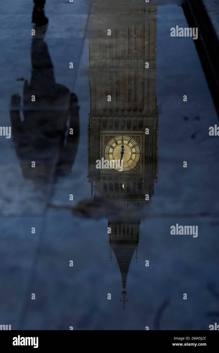 A commuter is reflected in a puddle with the Queen Elizabeth Tower in ...