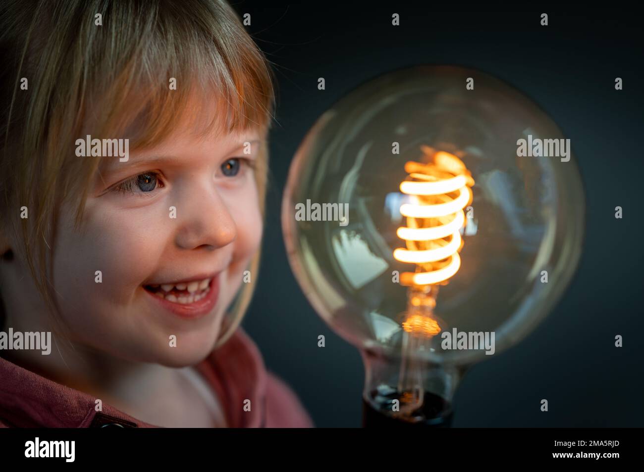 Happy child looks curious to a huge filament light bulb. Symbol for a ...