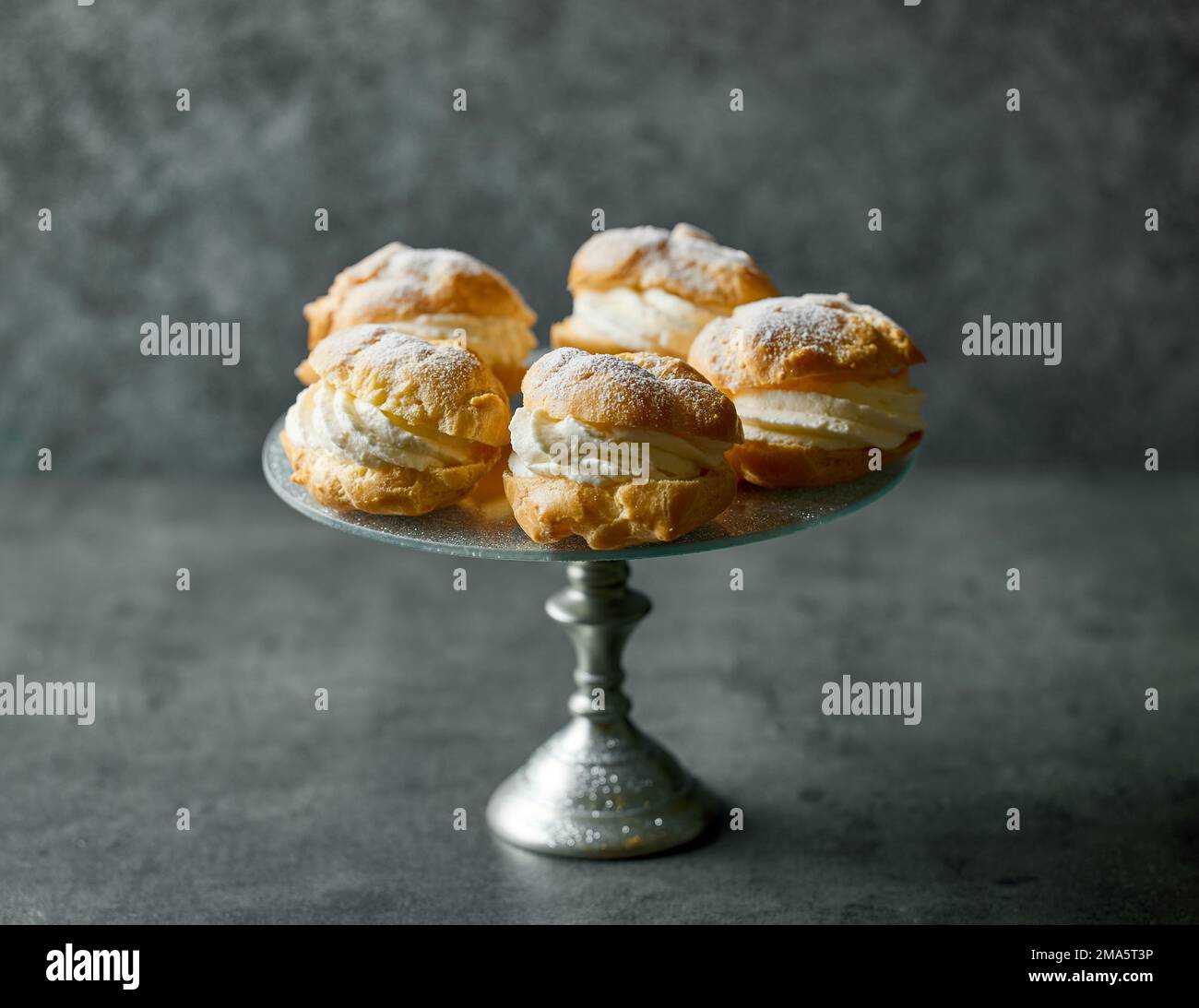 plate of cream puffs decorated with powdered sugar on dark grey ...