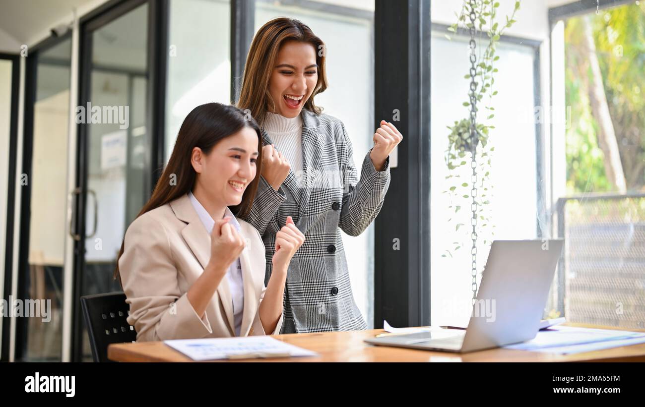 Two cheerful and excited millennial Asian businesswomen celebrating ...
