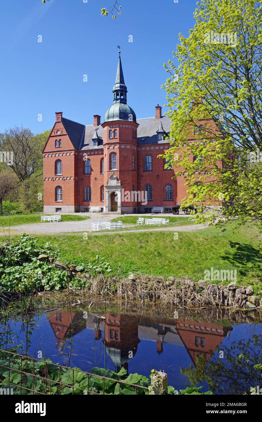 Red manor house reflected in a ditch, Skovsgard God, Langeland, Denmark ...