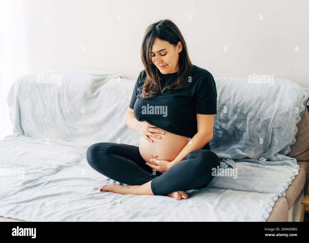 A middle-aged pregnant woman carefully hugs her belly while sitting on ...