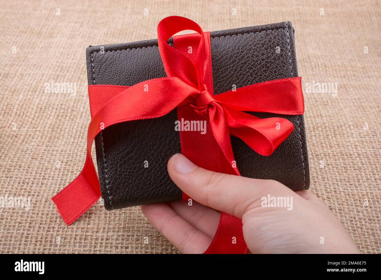 Hand holding a gift wallet wrapped with red ribbon Stock Photo - Alamy