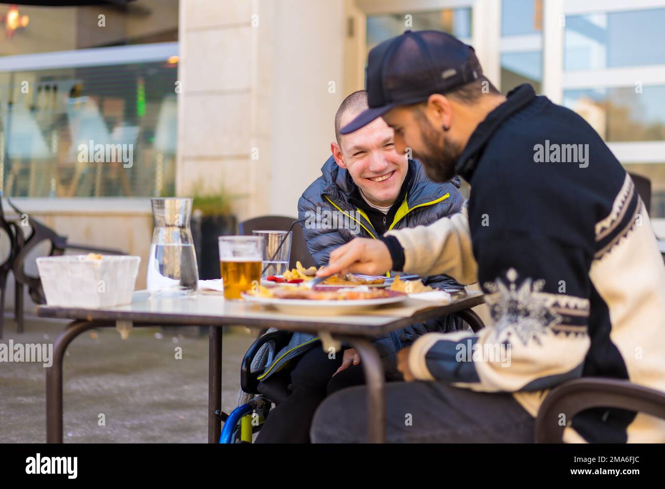 A disabled person eating and smiling with a friend having fun, terrace ...