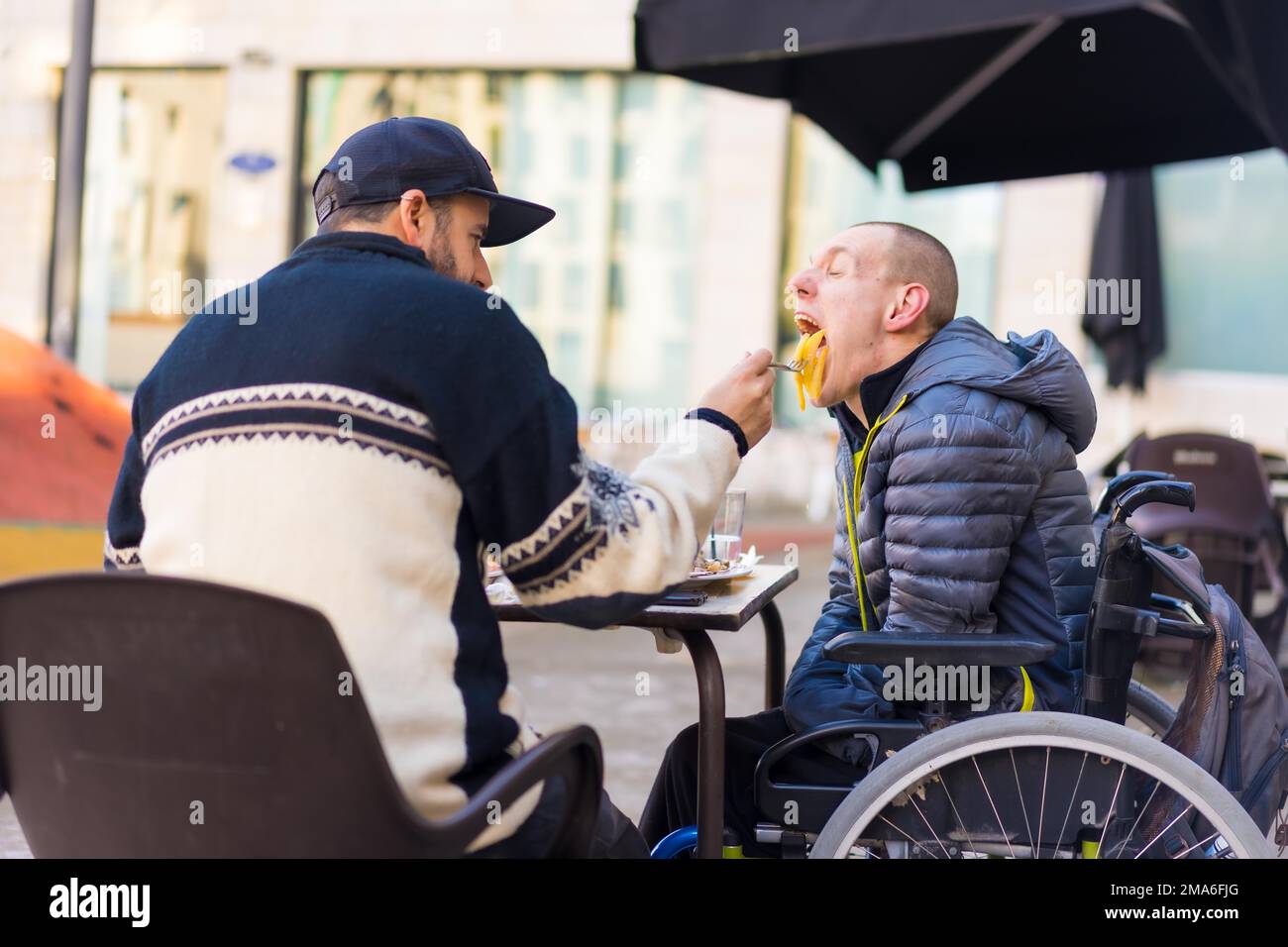 A disabled person eating with the help of a family member having fun ...