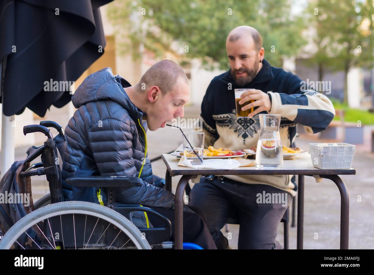 A disabled person eating on the terrace of a restaurant with a friend ...