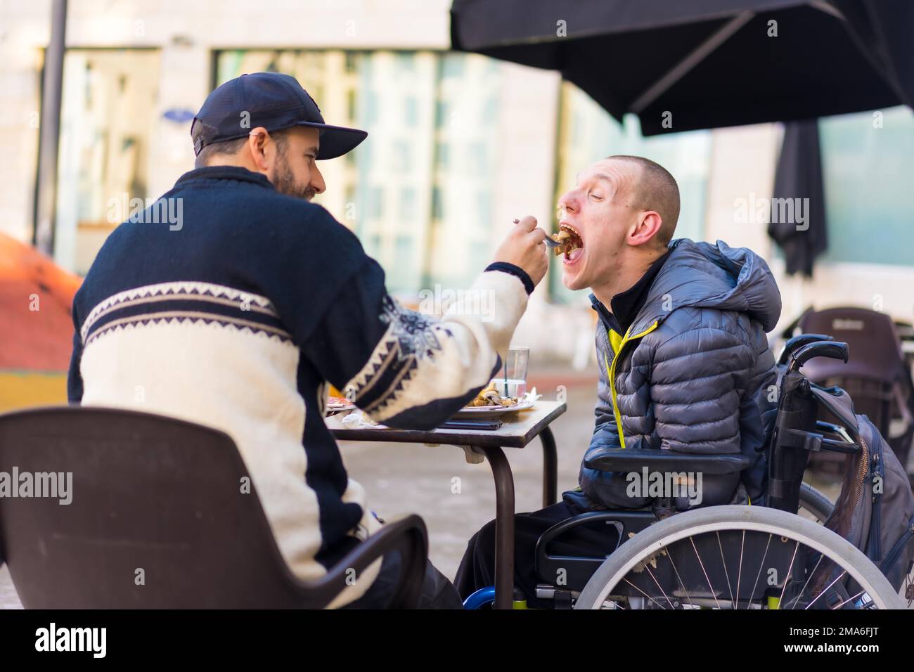 A disabled person eating with the help of a brother having fun, terrace ...