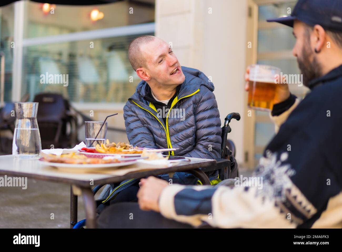 A disabled person eating and smiling with a friend having fun, terrace ...