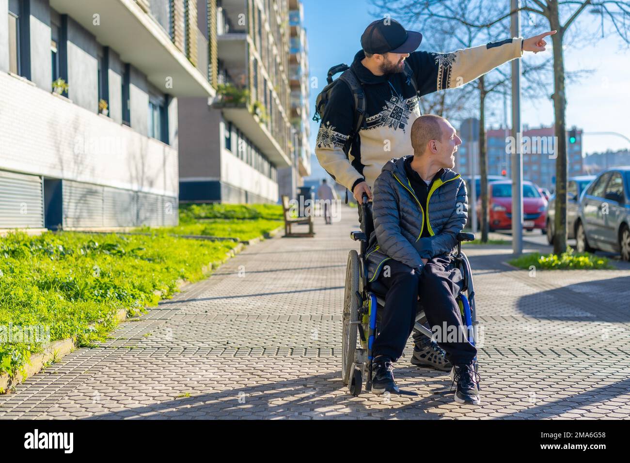 A disabled person in a wheelchair walking with a friend in a chair on ...