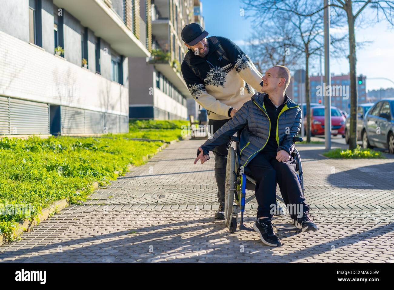 A disabled person in a wheelchair walking with a friend in a chair on ...